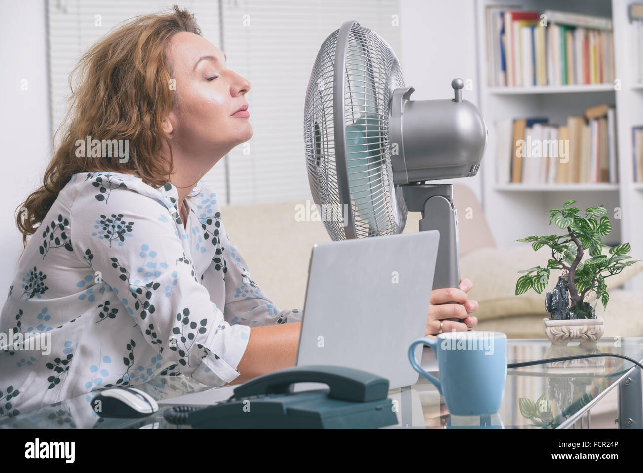 Woman suffers from heat while working in the office and tries to cool ...