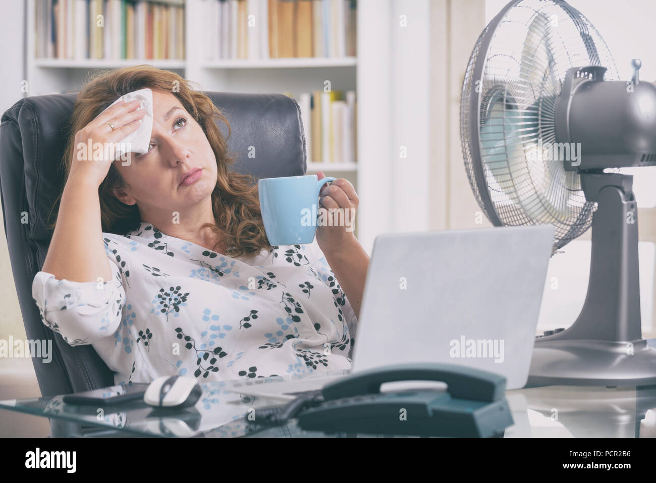 Woman suffers from heat while working in the office and tries to cool ...