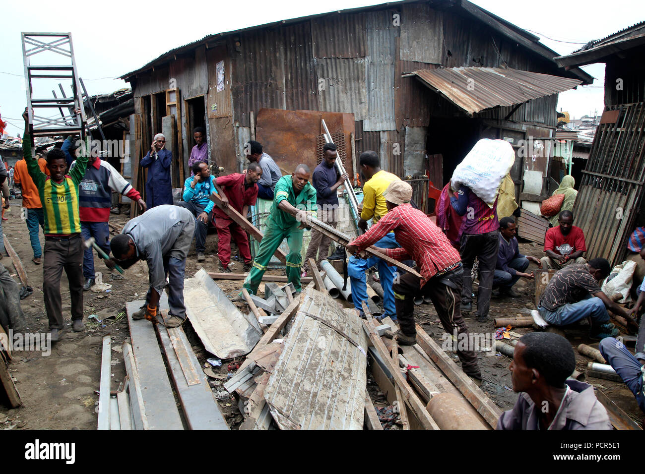 Men in front of corrugated-iron huts, build market stall of metal scrap ...