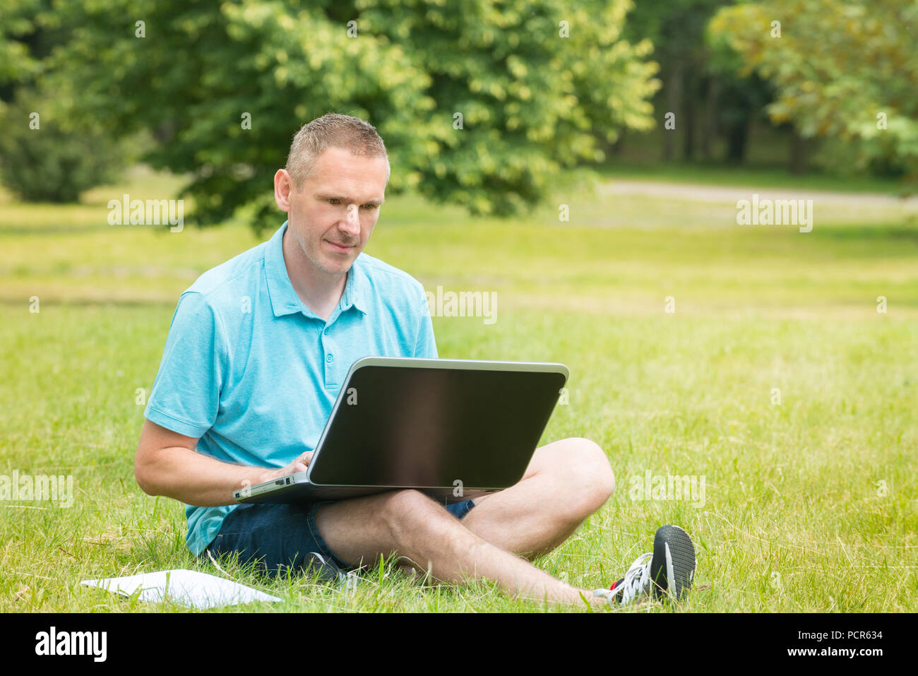 Man sitting on grass in the park and working on his laptop Stock Photo ...