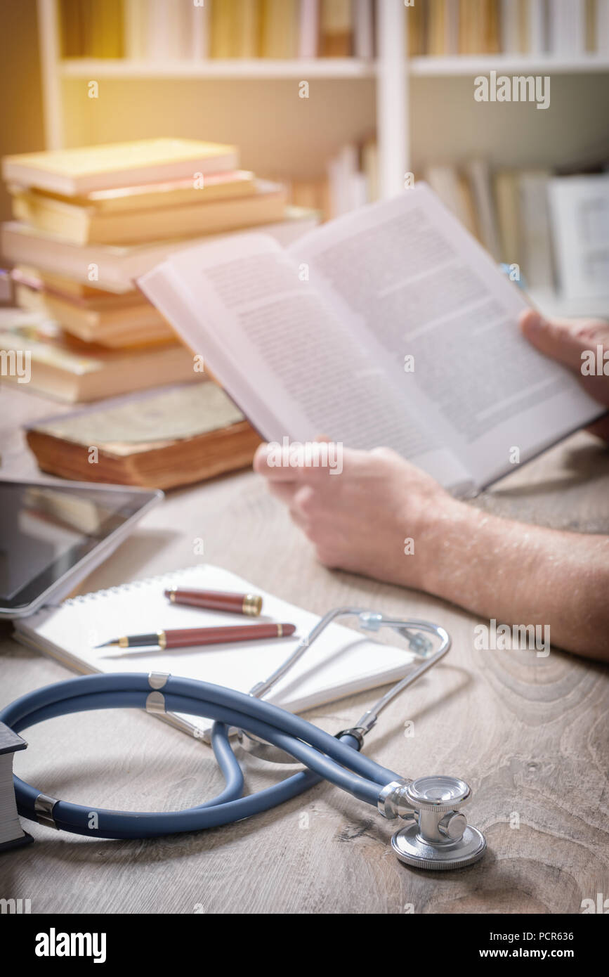 Young doctor is learning and preparing for the exam, he is using books ...