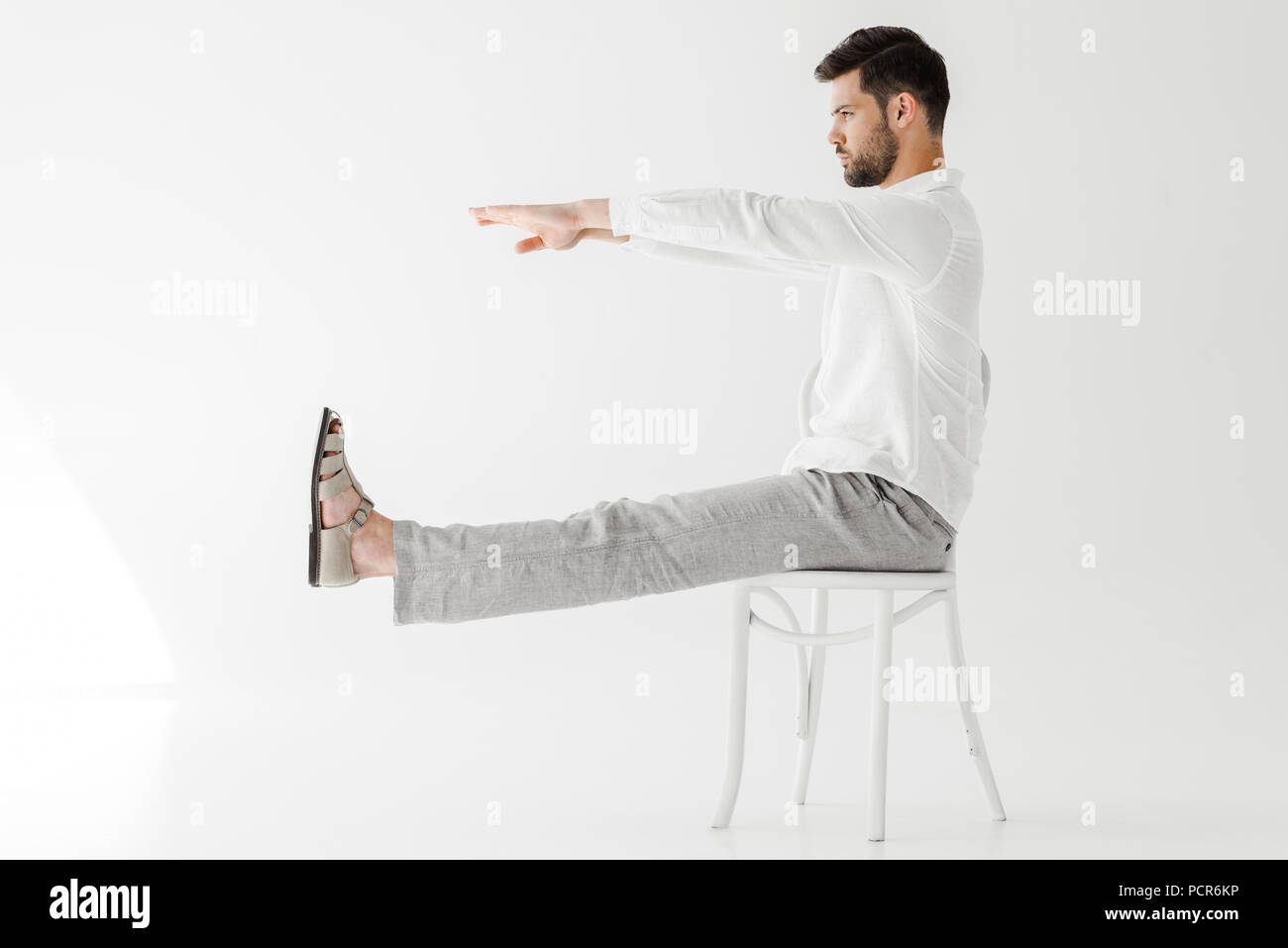 side view of male model in linen clothes sitting on chair with ...