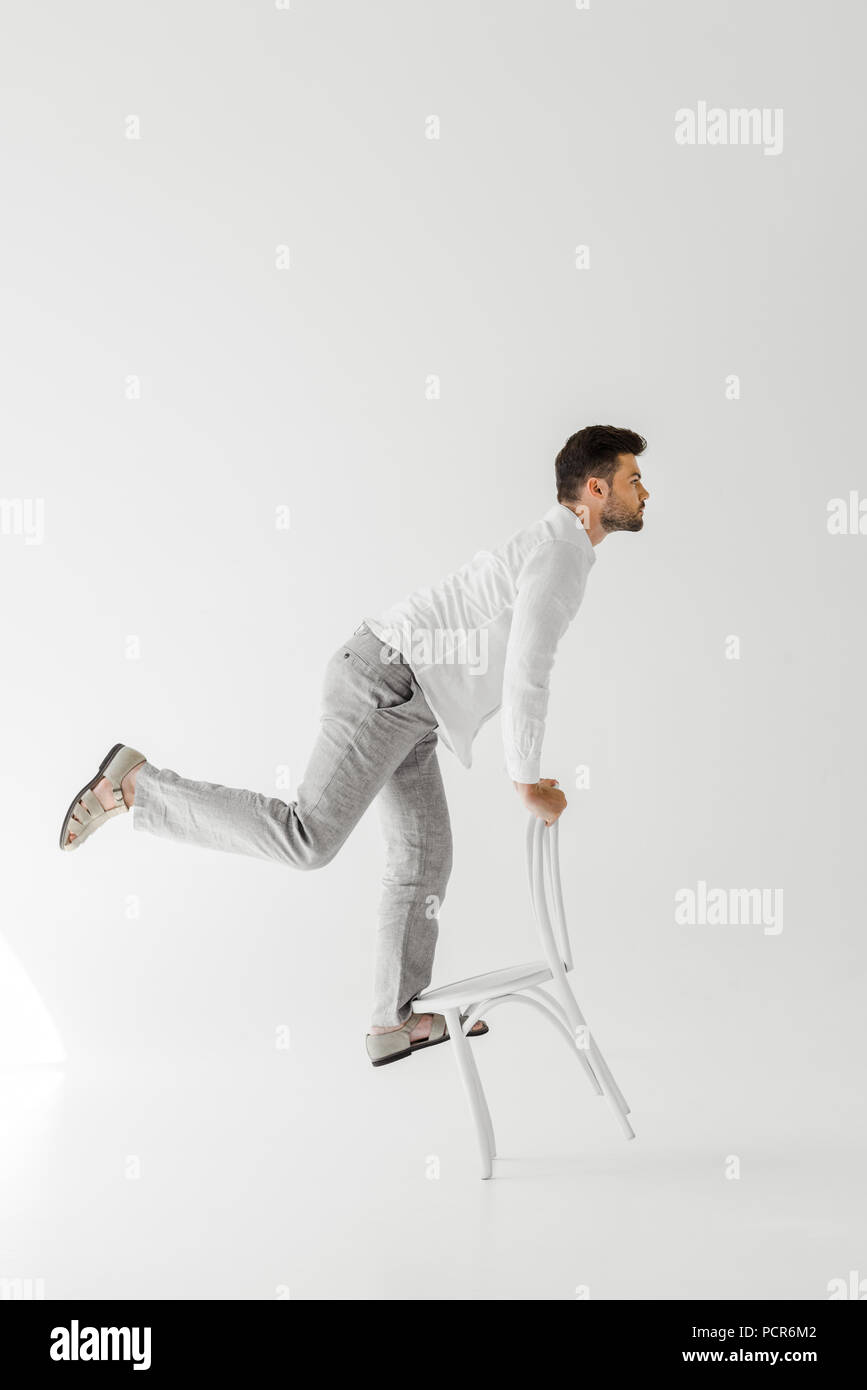 side view of man in linen clothes balancing on chair isolated on grey ...