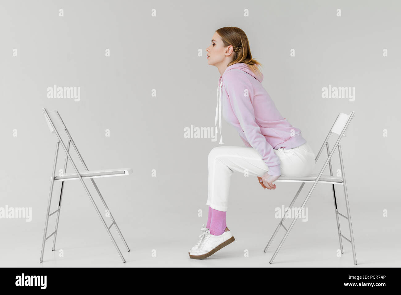 side view of stylish young woman sitting on chair in front of another ...