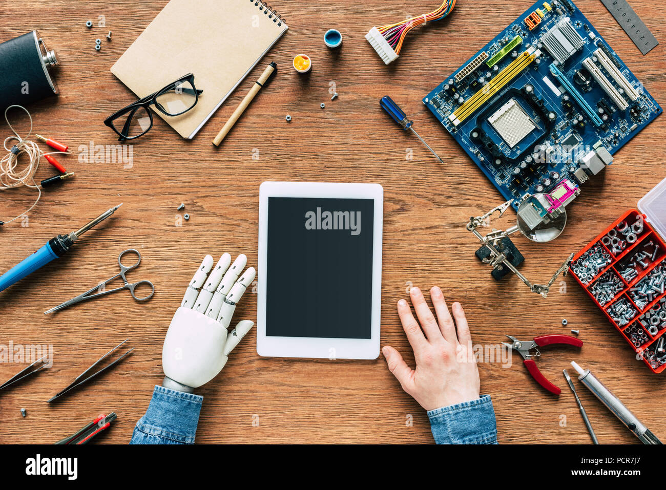 cropped image of electronic engineer with robotic hand sittng at table ...