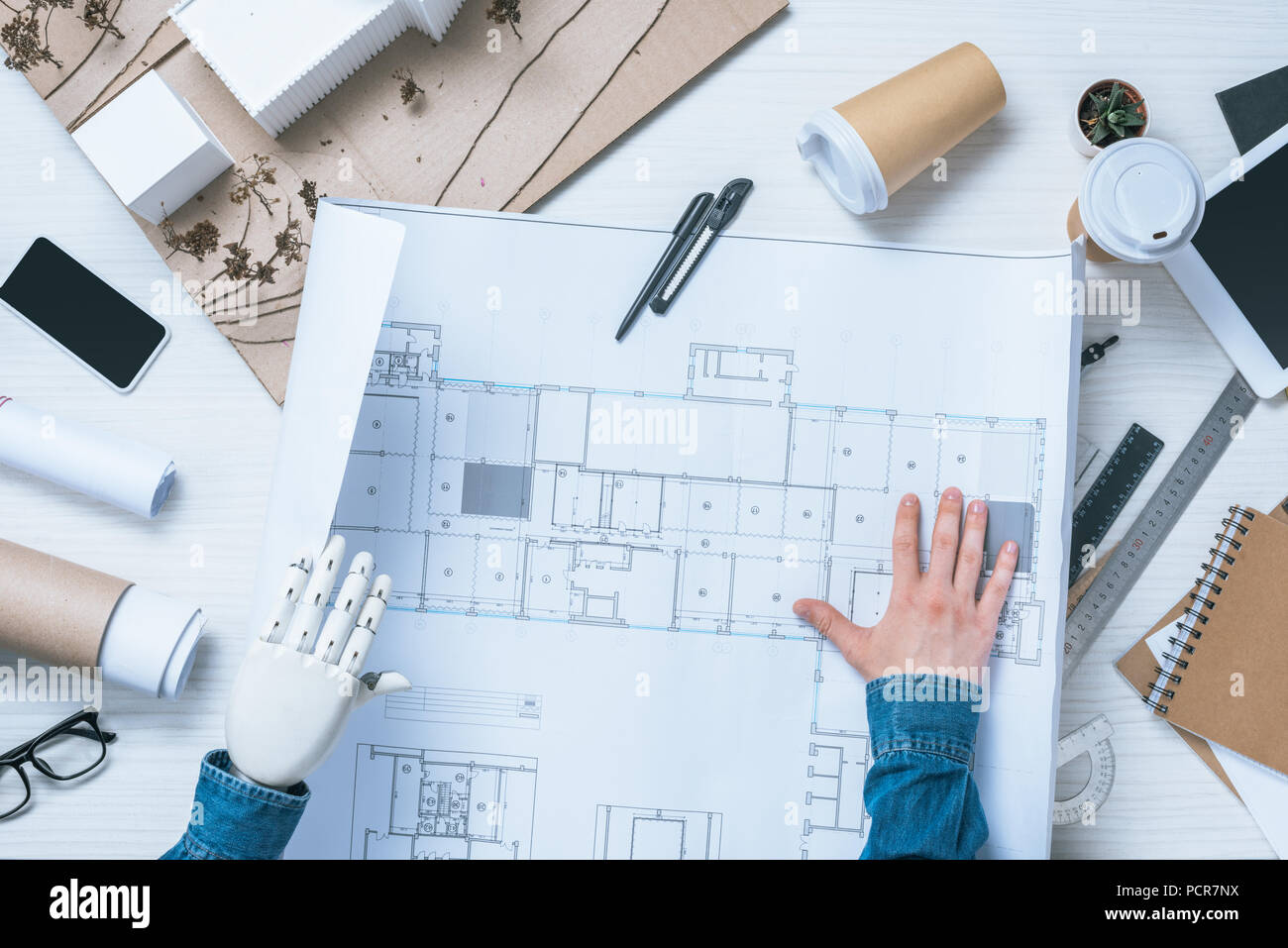 partial view of male architect with prosthetic arm looking at blueprint ...