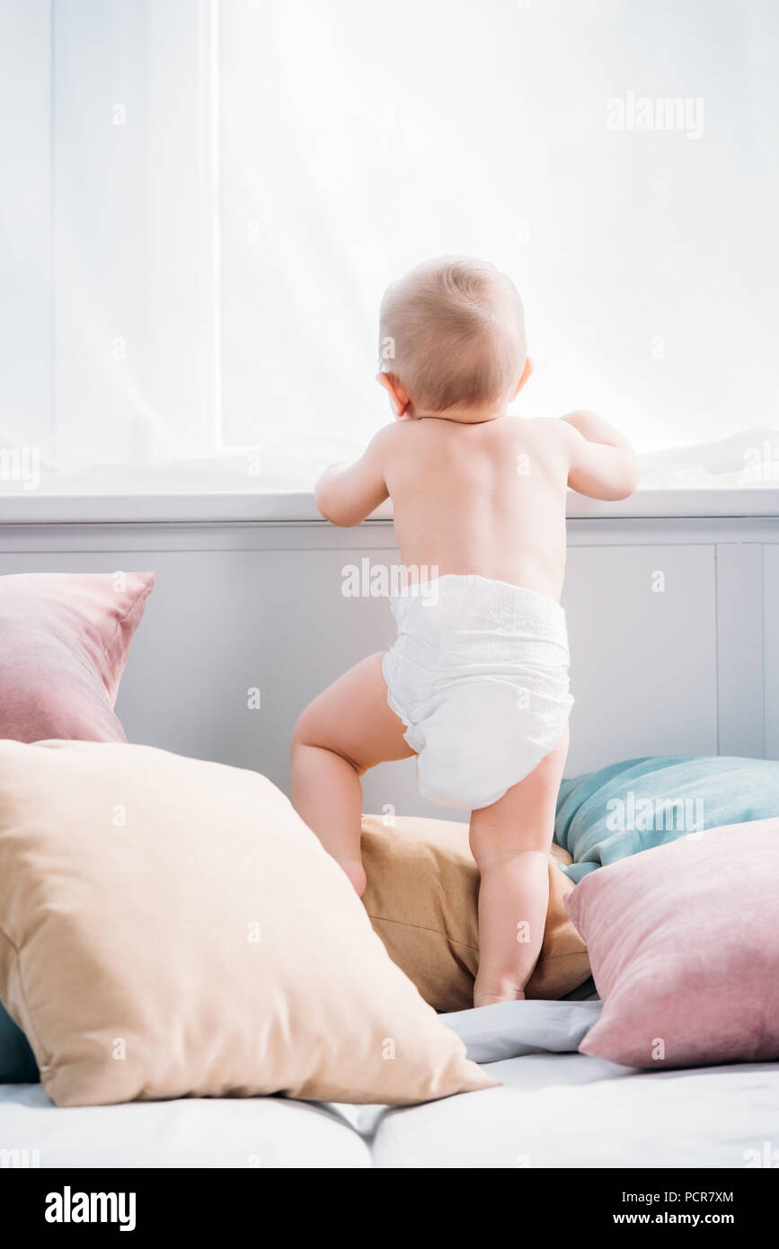 happy little baby standing on bed with lot of pillows and looking ...
