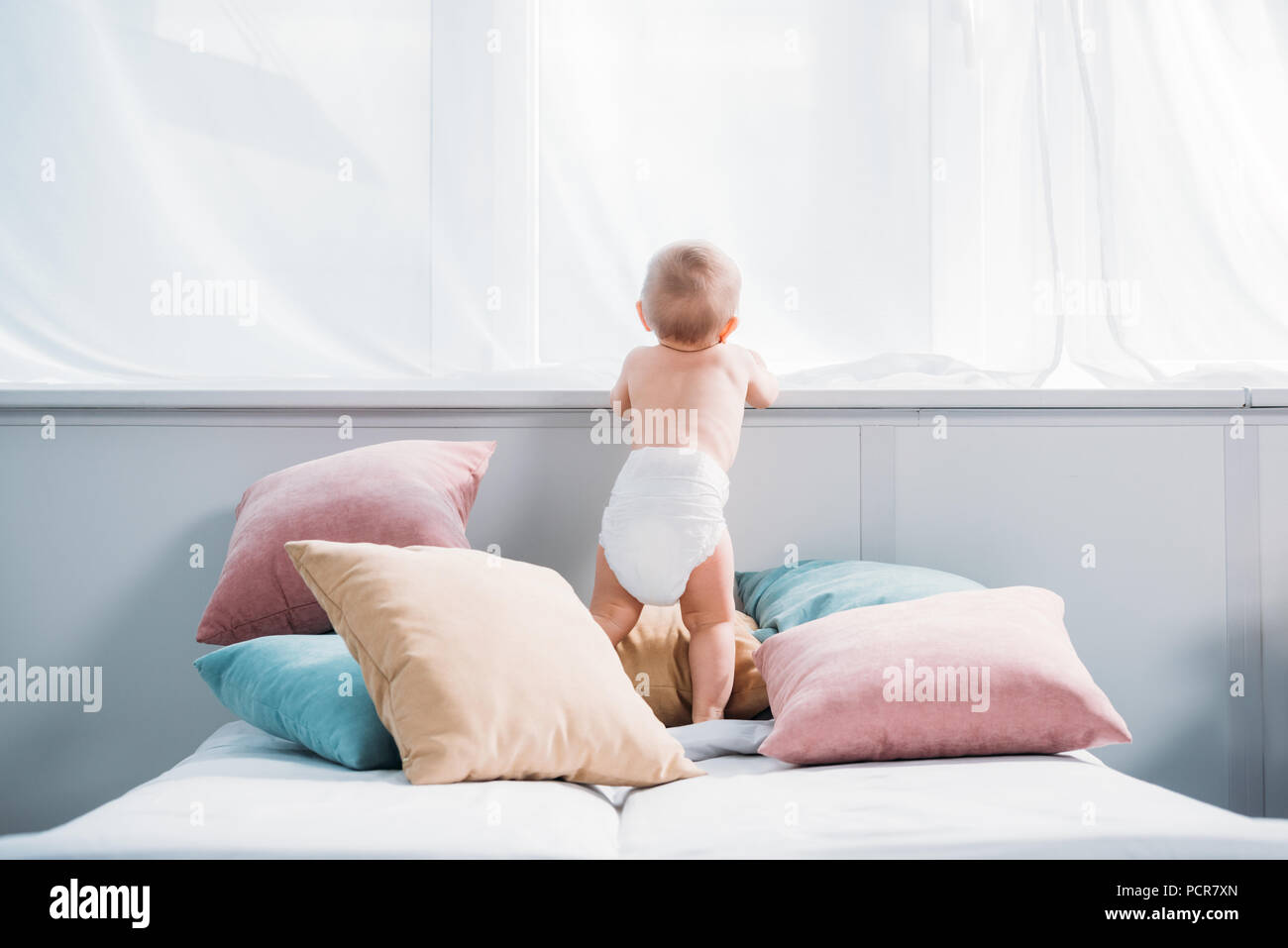 happy little baby in diaper standing on bed with lot of pillows and ...