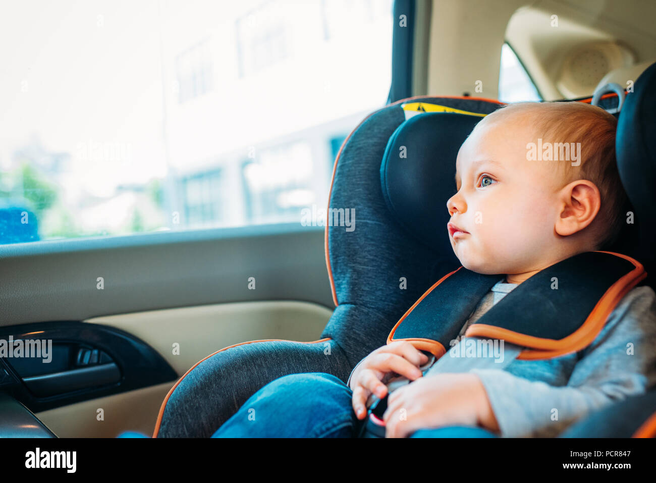 adorable little baby sitting in child safety seat in car and looking ...