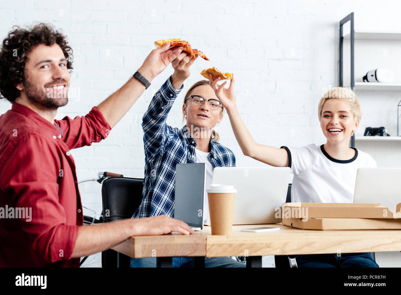 happy young business colleagues eating pizza and smiling at camera ...