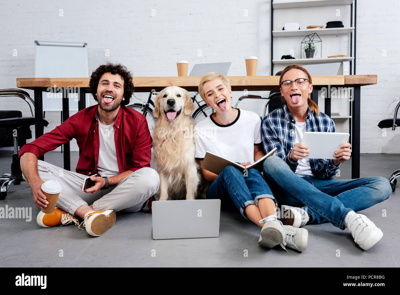 happy young business colleagues and dog sitting on floor with tongues ...
