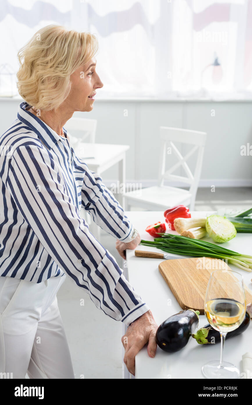 side view of attractive grey hair woman leaning on kitchen counter ...
