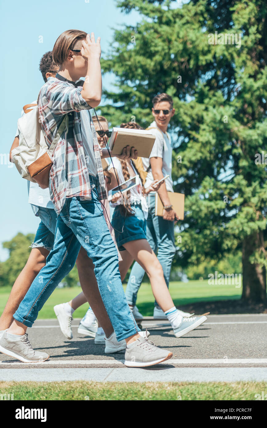 side view of teenage students with books and gadgets walking together ...