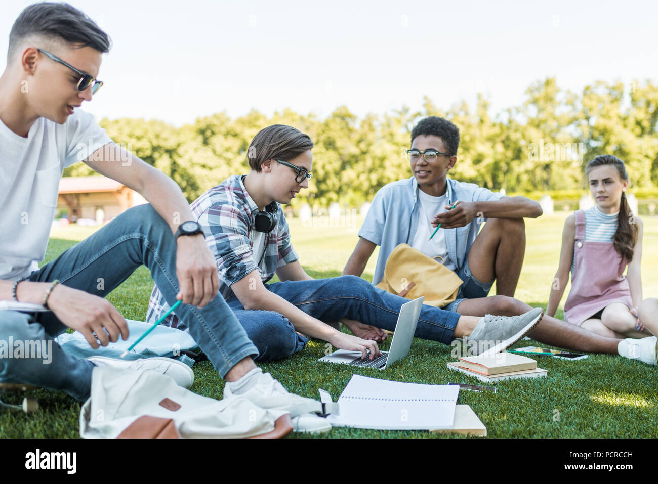 happy multiethnic teenagers sitting and talking while studying together ...