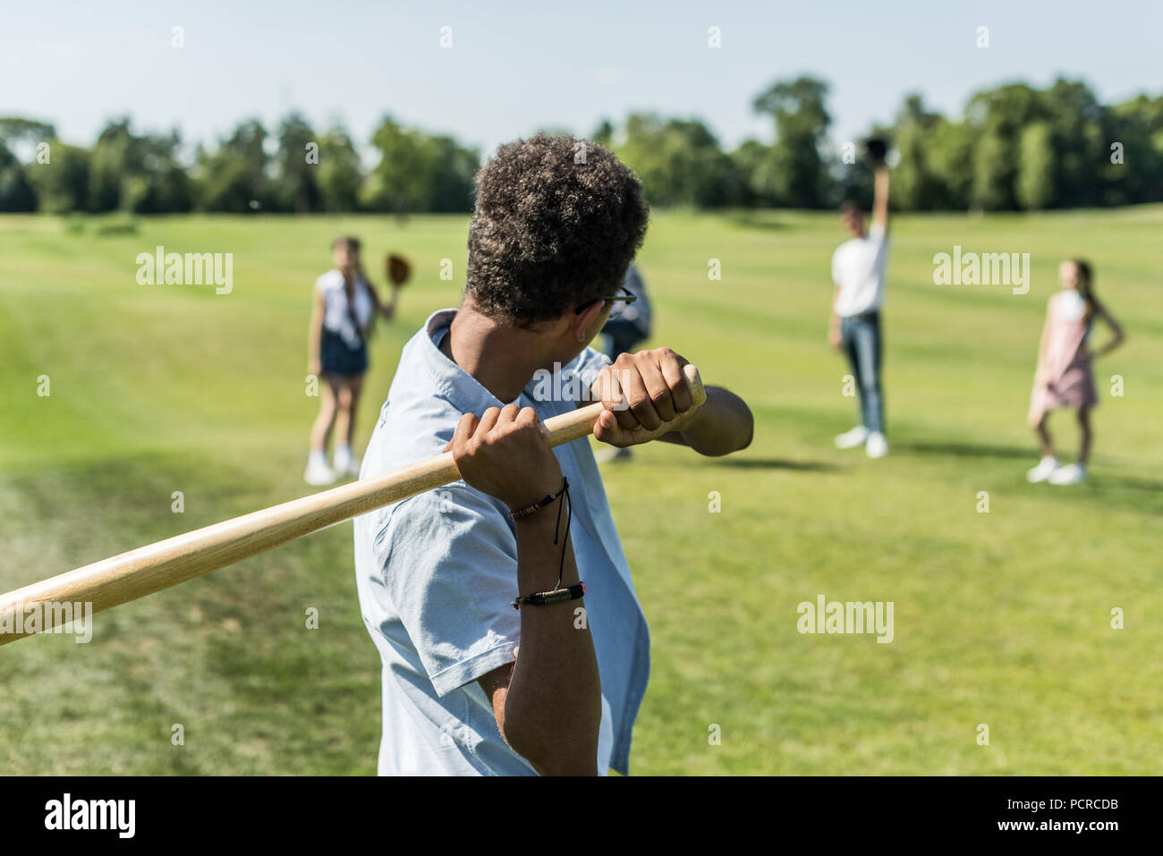 teenage african american boy playing baseball with friends in park ...
