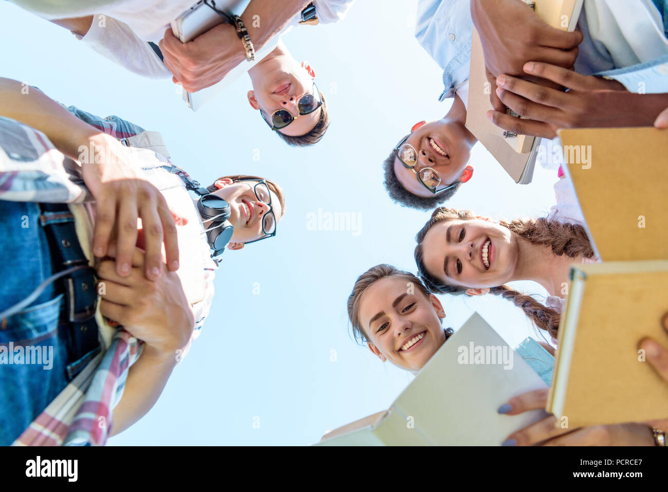 bottom view of happy teenage multiethnic friends holding books and ...