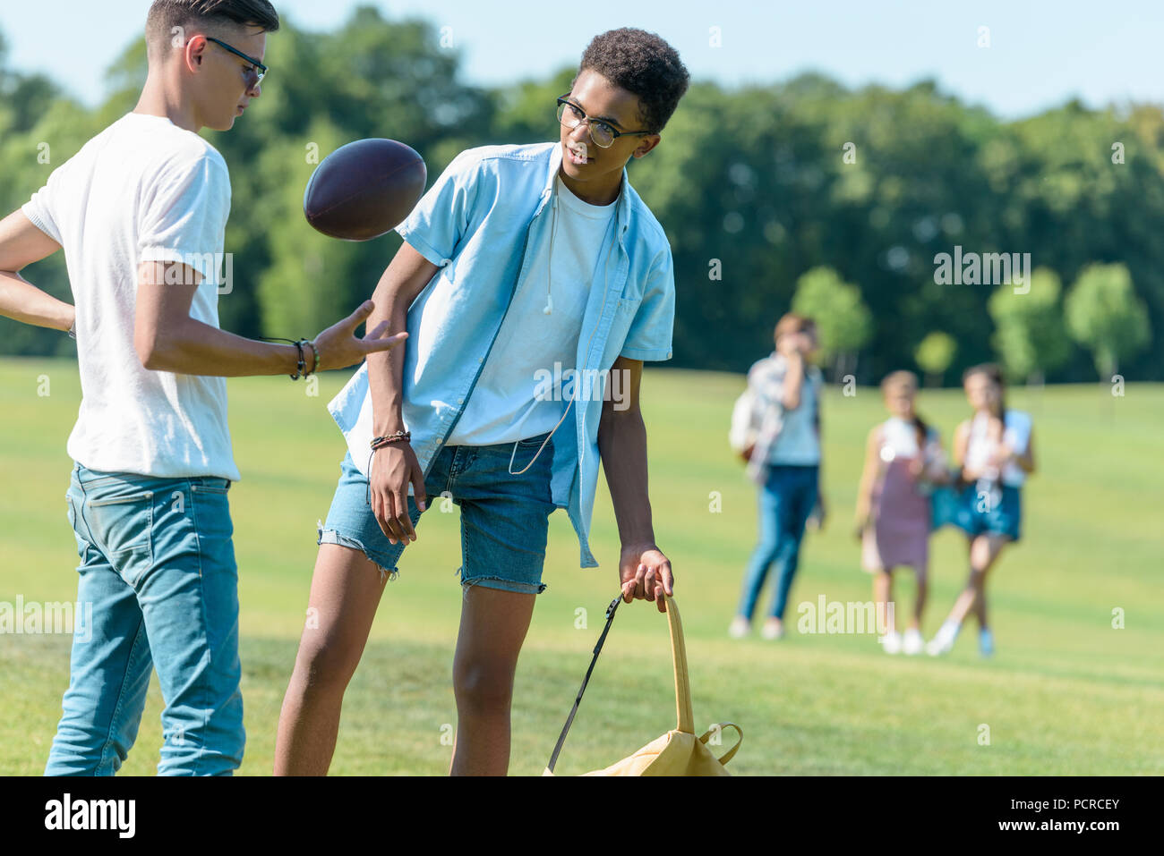 teenage multiethnic friends playing with rugby ball while classmates ...