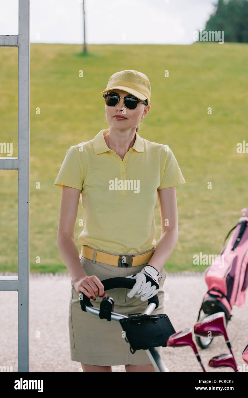 portrait of female golf player in cap and sunglasses standing near golf ...