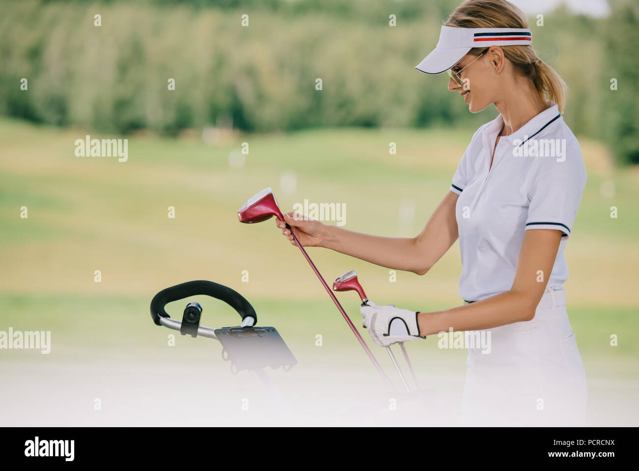 selective focus of smiling female golf player in cap with golf gear at ...
