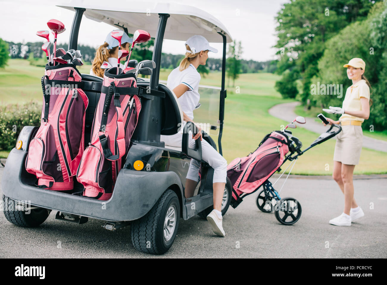 smiling female golf players at golf cart getting ready for game at golf ...