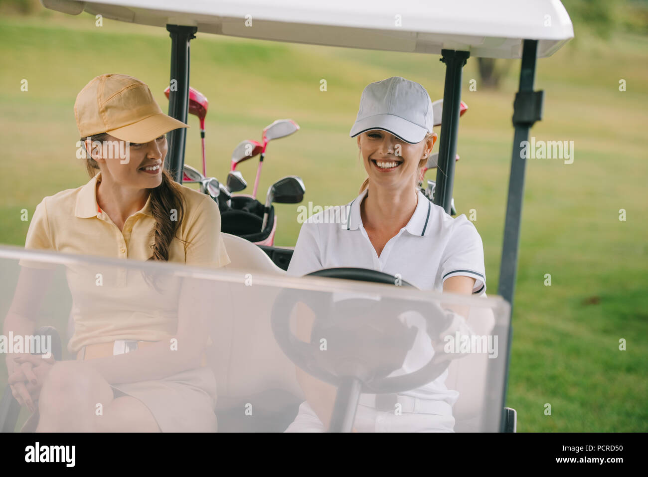 smiling female golf players riding golf cart at golf course Stock Photo ...
