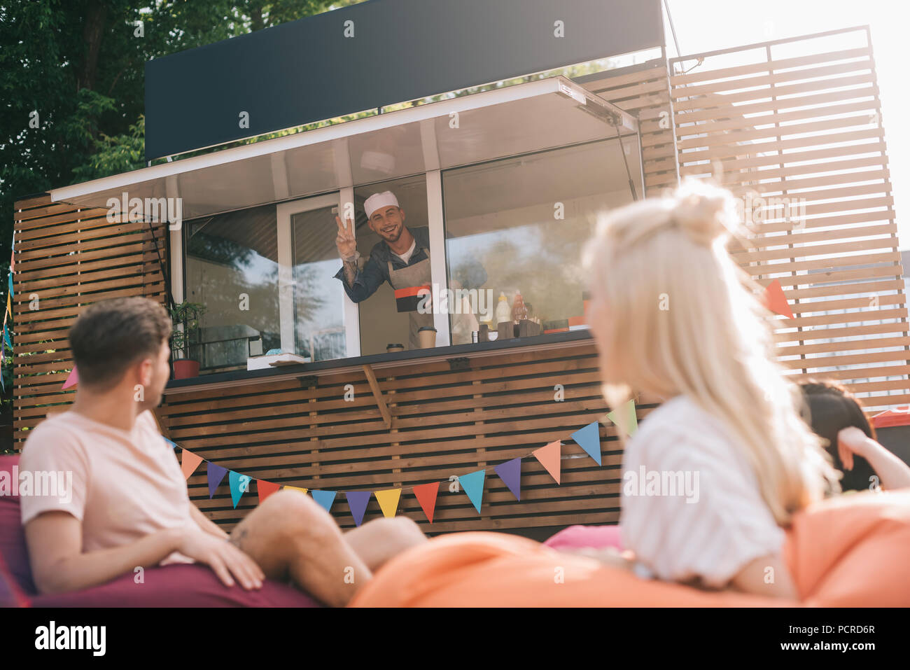 happy chef working in food truck and smiling to young customers outside ...