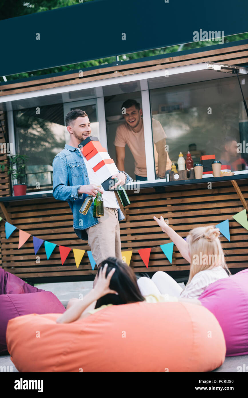man carrying boxes with fast food and bottles of beer to friends near ...