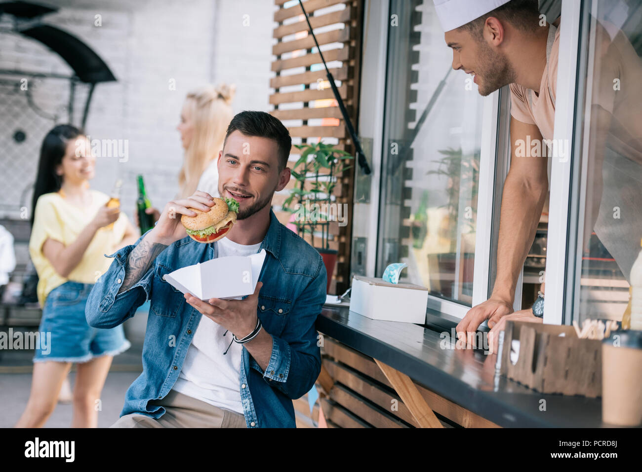 handsome man eating burger near food truck Stock Photo - Alamy