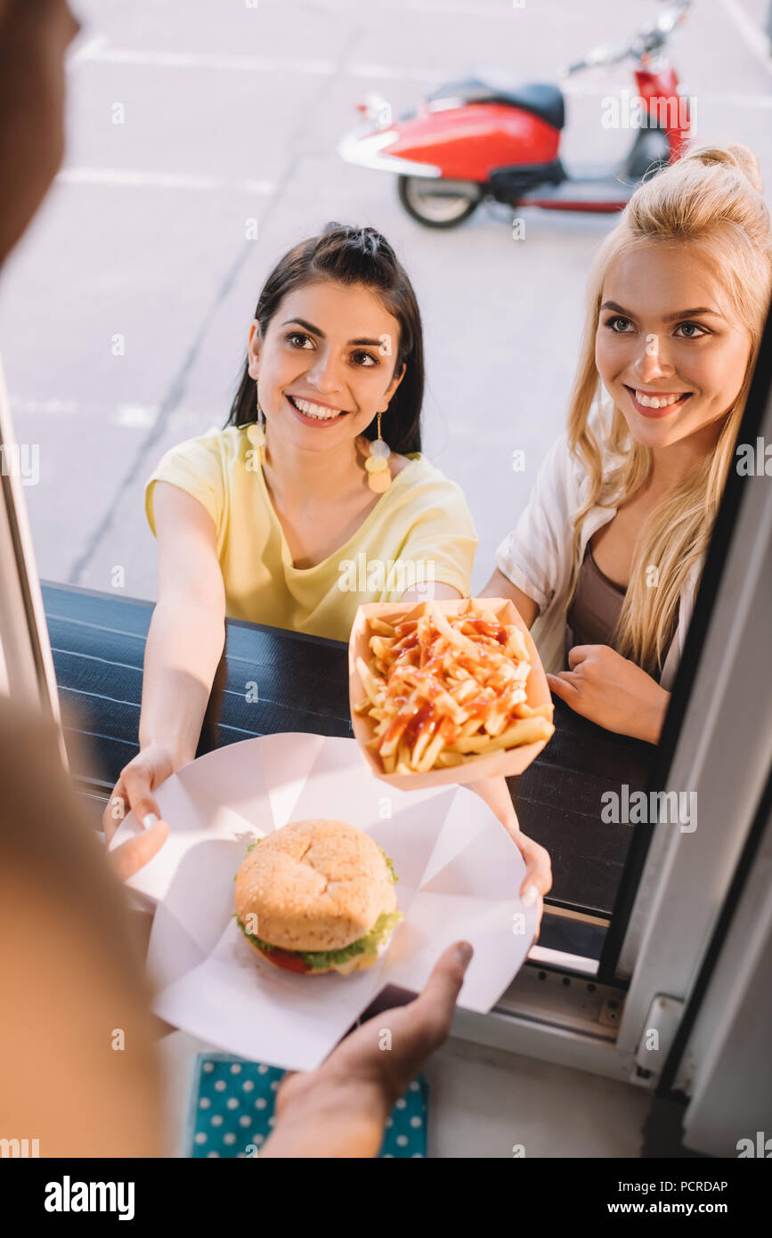 cropped image of chef giving burger and french fries to smiling ...