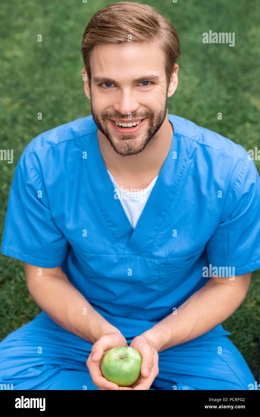 smiling handsome medical student holding apple in hands and looking at ...