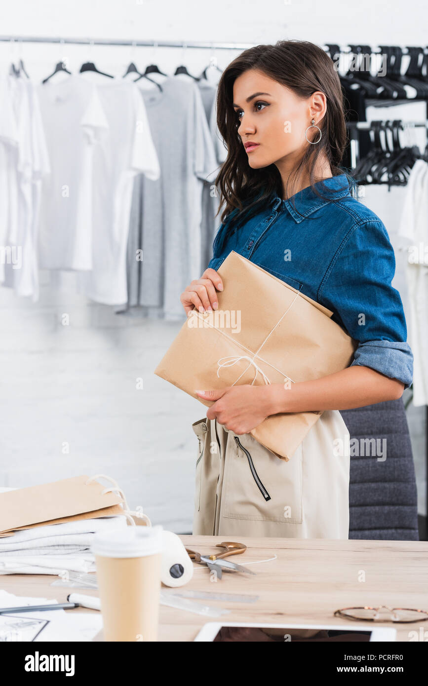 side view of female designer holding paper package in clothing design ...