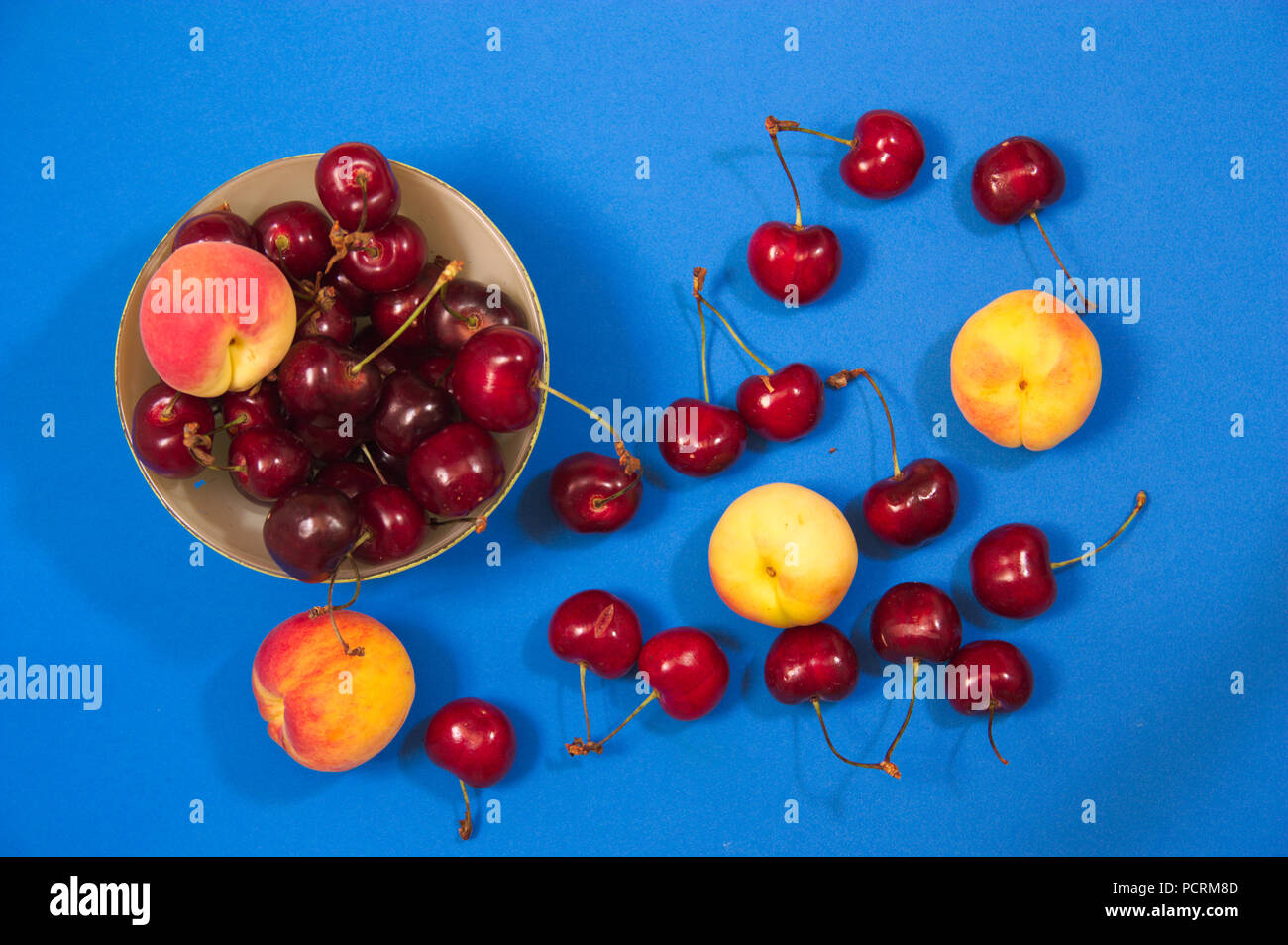 Some apricots and cherries on a table of intense blue color Stock Photo ...