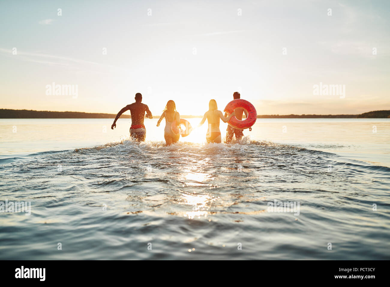 Rearview of a diverse group of friends in swimwear running into a lake ...