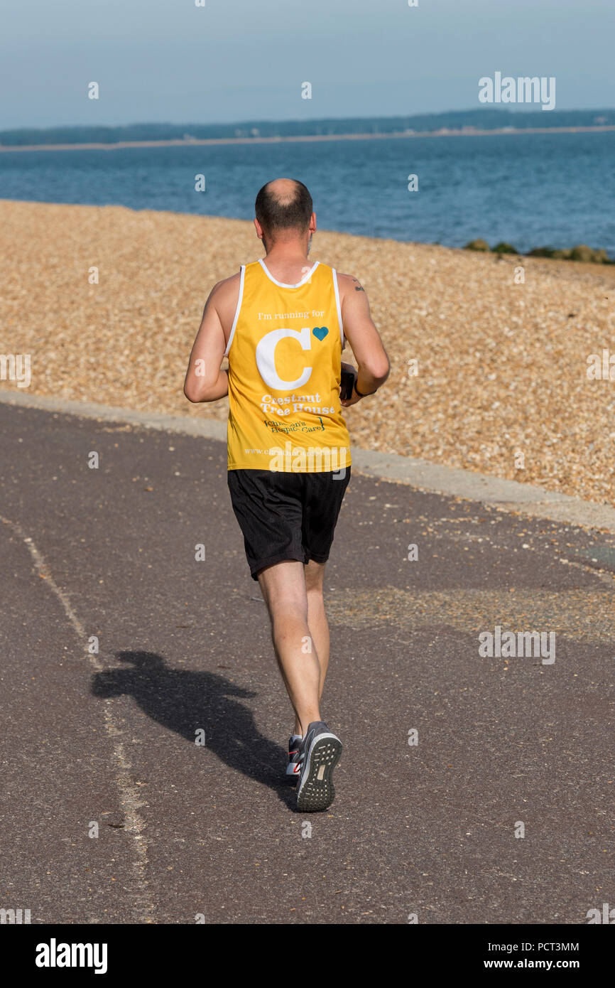 an older or middle aged man running along the seafront or beach at ...