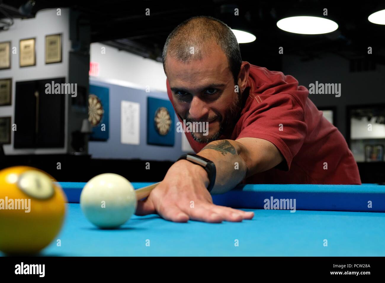 A pool player confidently lines up behind the cue ball to take aim just ...