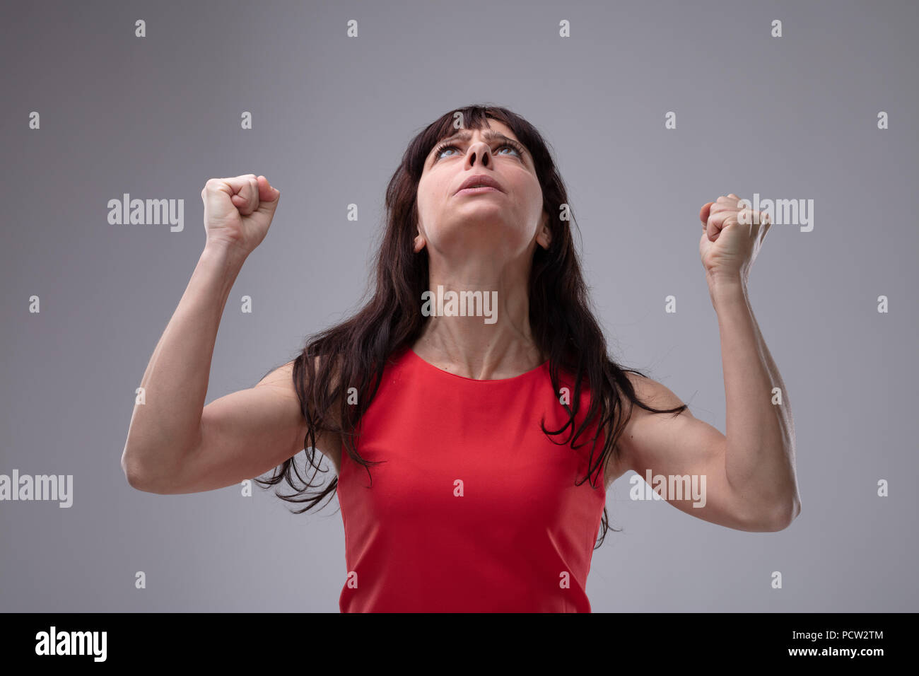Angry woman clenching her fists in frustration and looking up into the ...