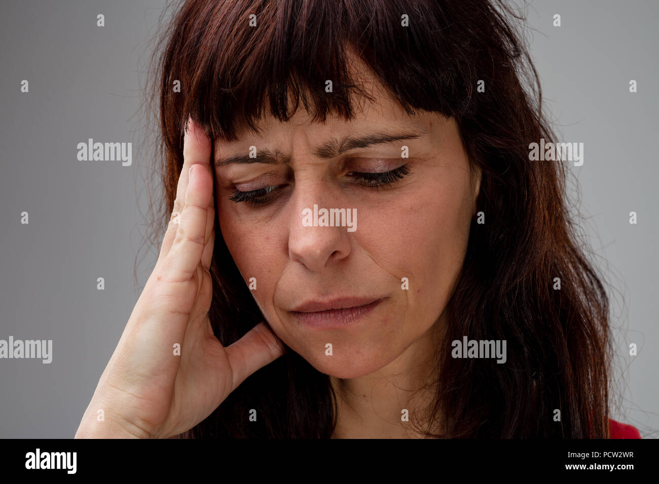 Worried woman with her hand to her head looking down and frowning with ...