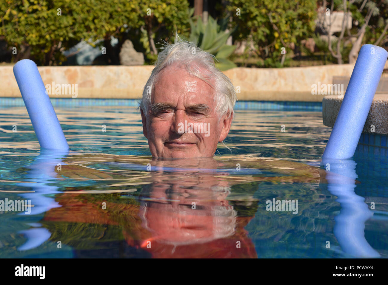 Senior man floating on a pool noodle in a swimming pool, portrait ...