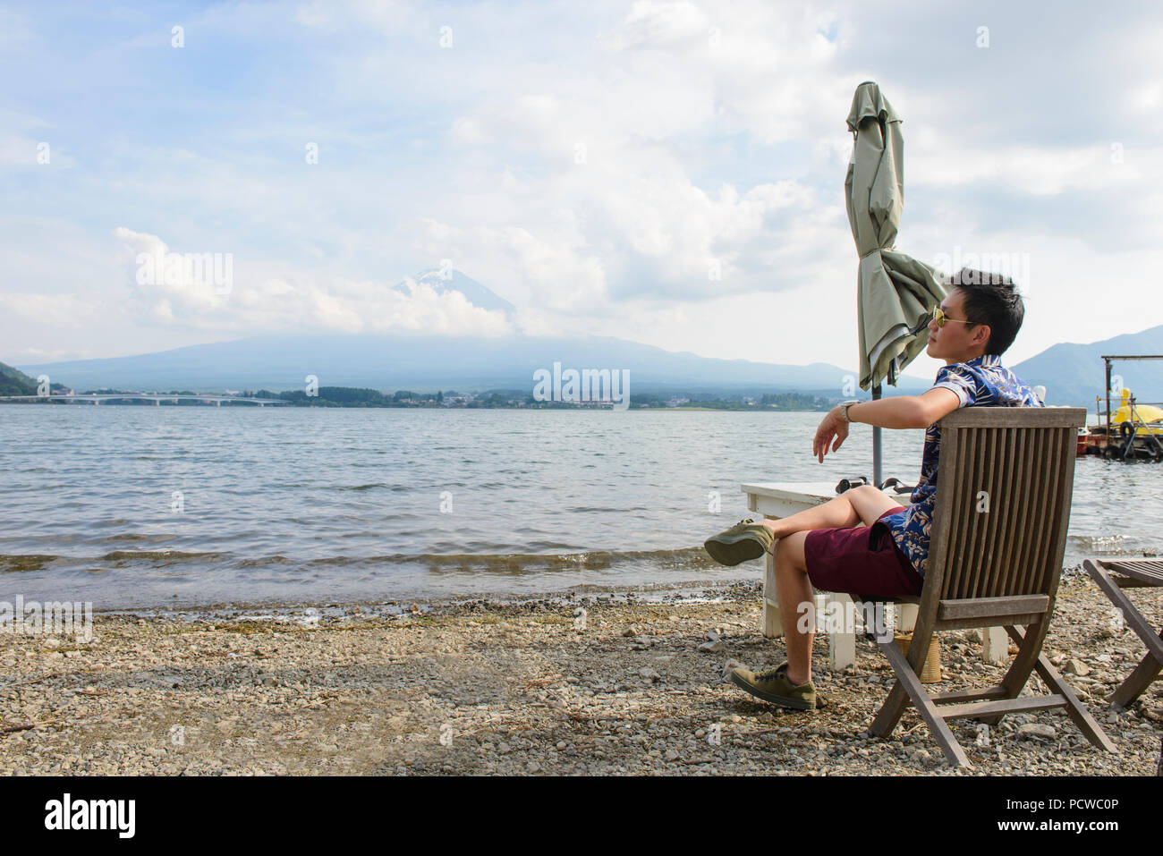 Asian man sitting on a chair at Kawaguchiko lake, Japan. View of fuji ...
