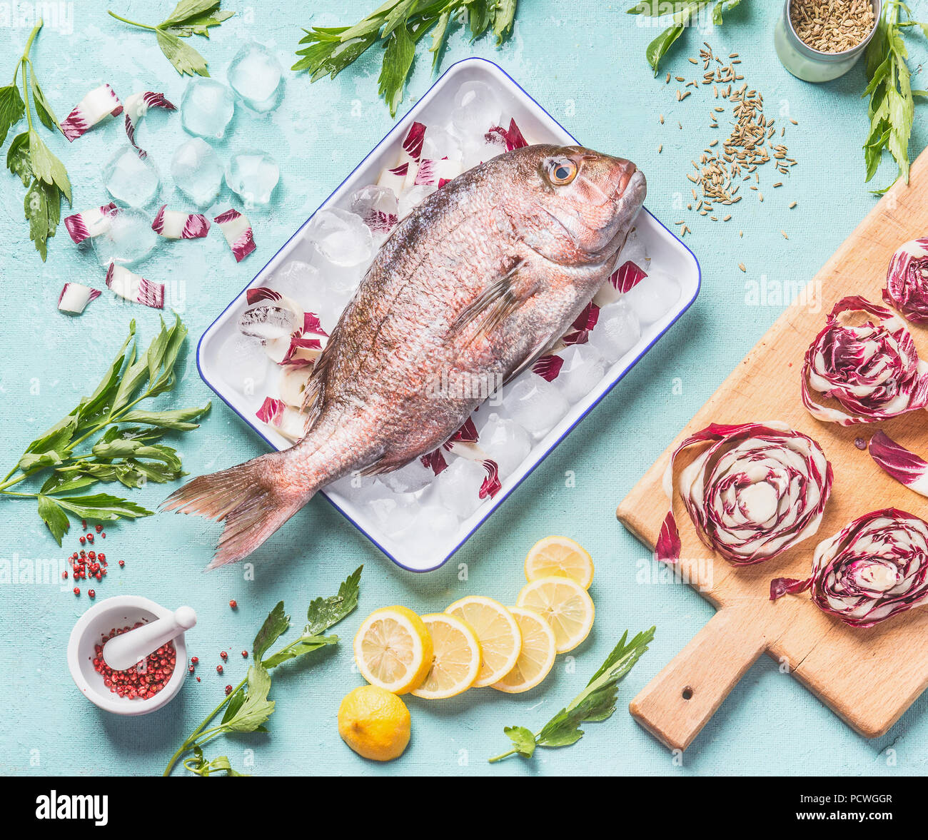 Raw whole fish in tray with ice cubes on light turquoise background ...