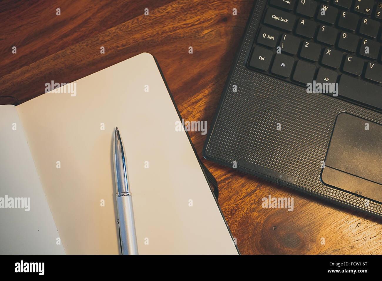 Blank note pad, silver metal pen and black laptop sitting on a solid ...