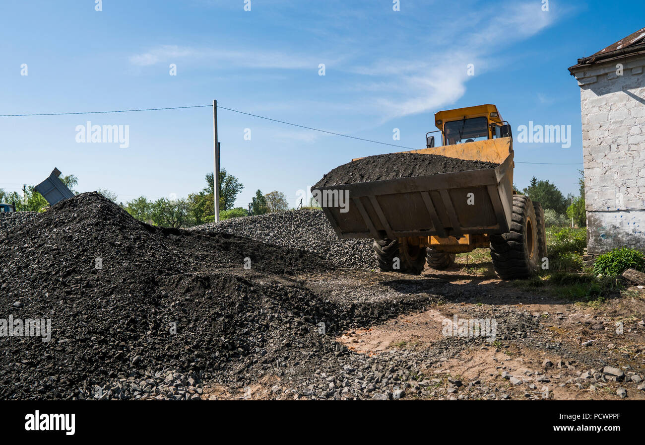 Yellow loader moving with uploaded bucket to the truck with stone ...