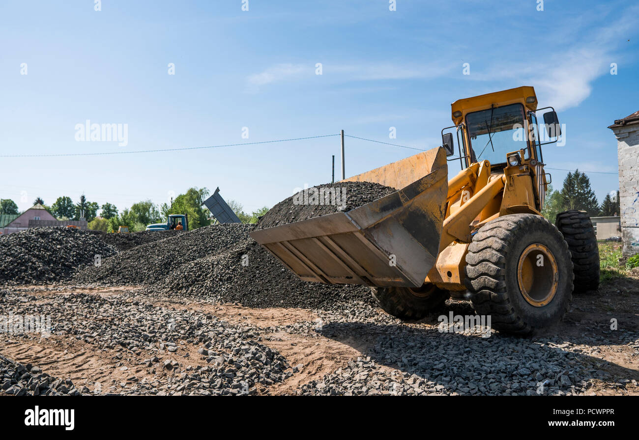 Yellow loader moving with uploaded bucket to the truck with stone ...