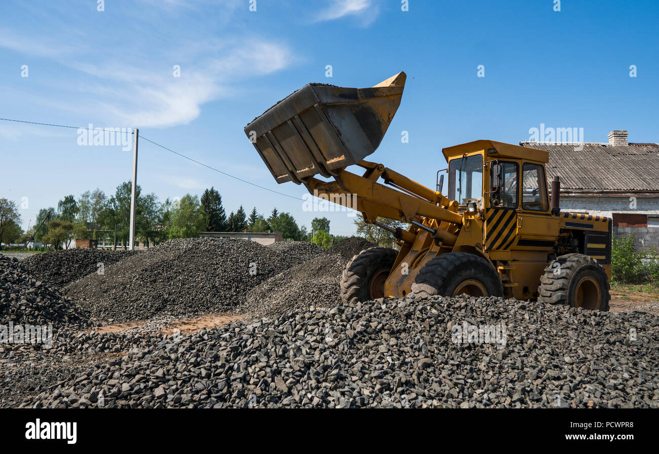 Yellow loader moving with uploaded bucket to the truck with stone ...