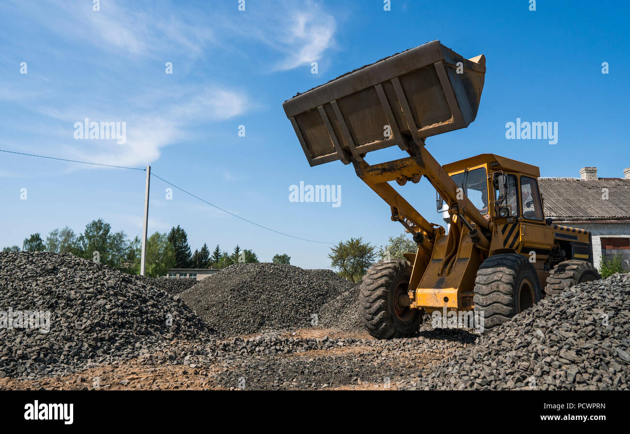 Yellow loader moving with uploaded bucket to the truck with stone ...