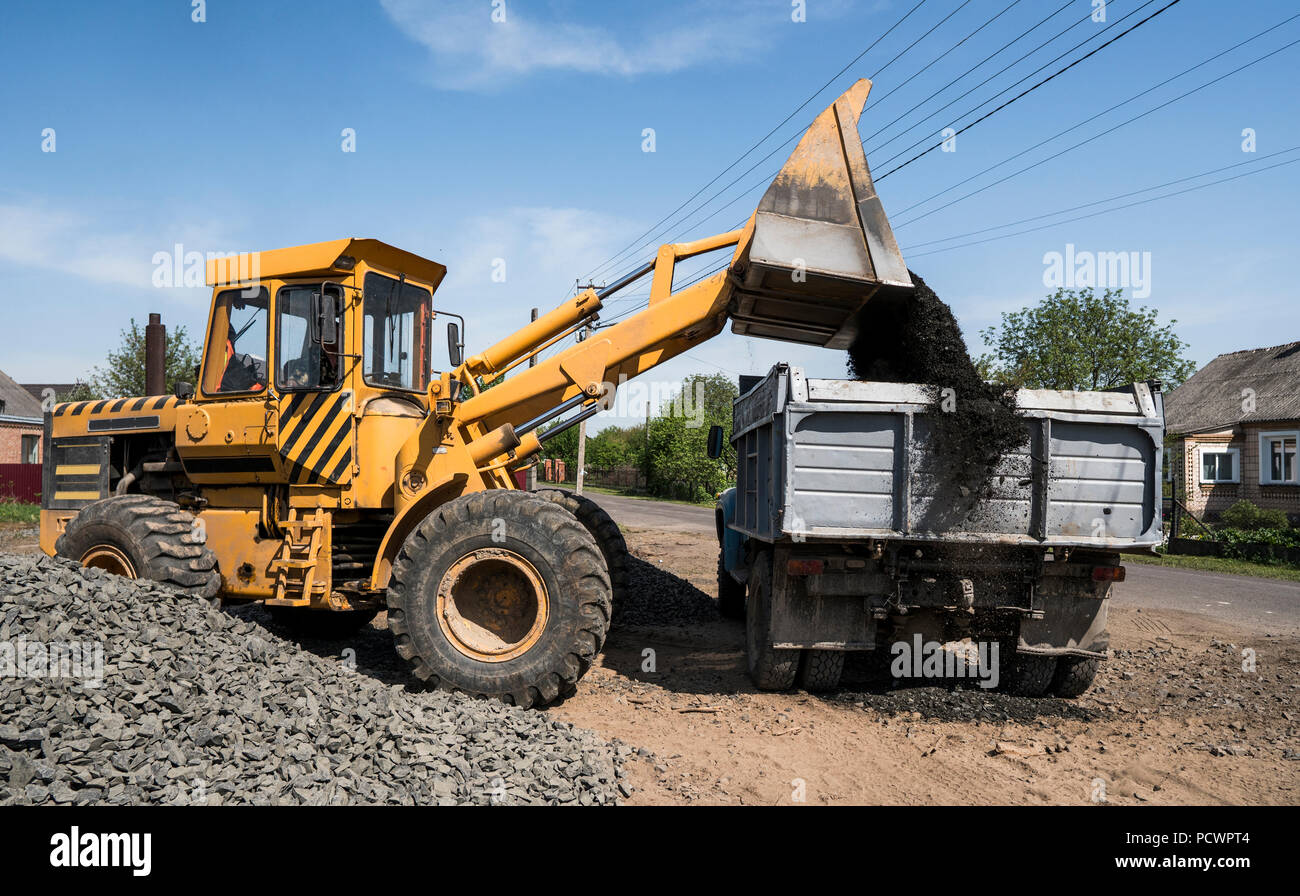 Yellow loader delivering stone gravel into truck during road ...