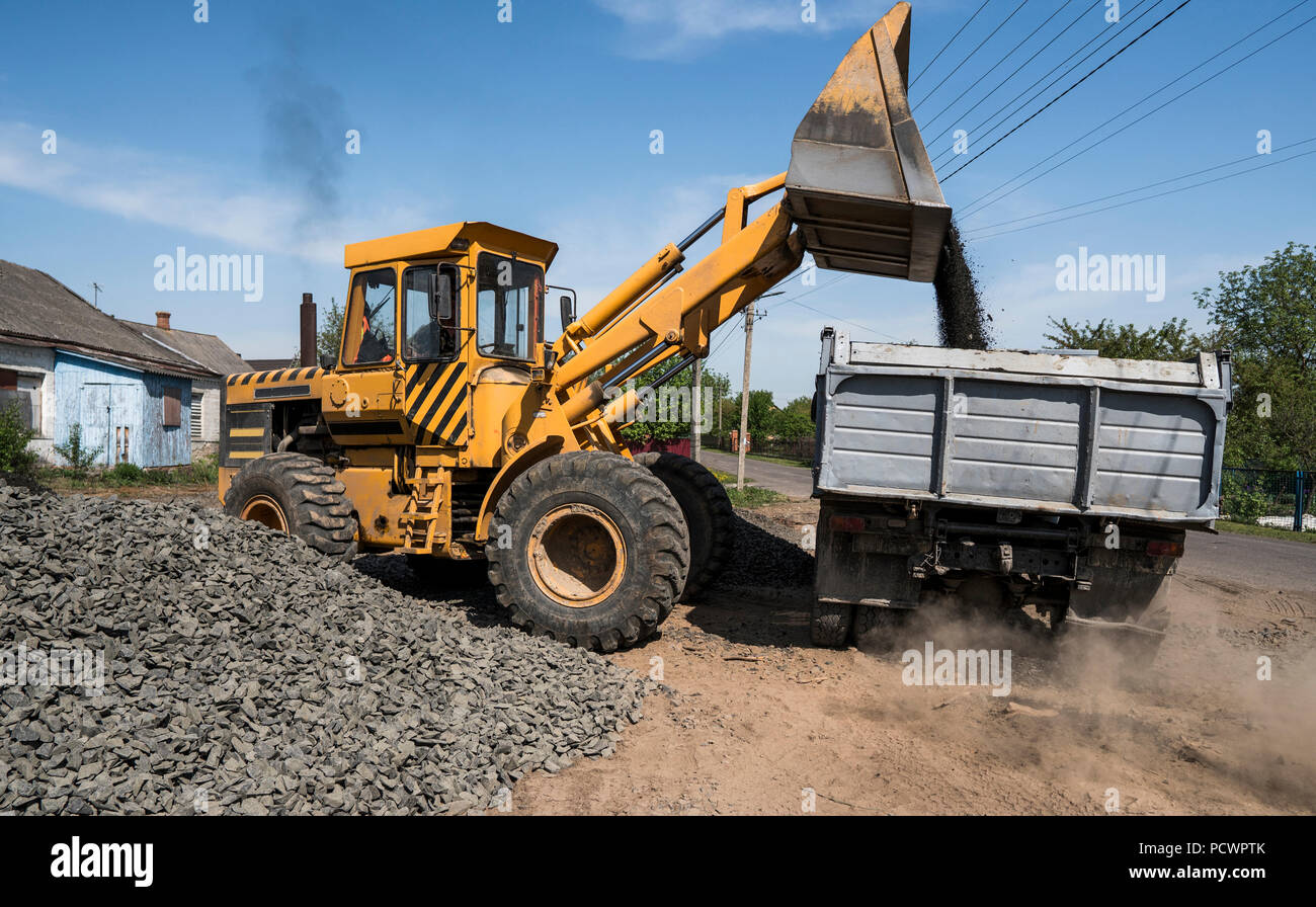 Yellow loader delivering stone gravel into truck during road ...