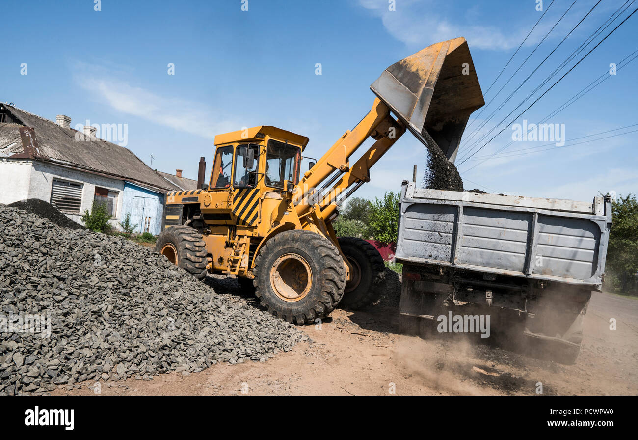 Yellow loader delivering stone gravel into truck during road ...