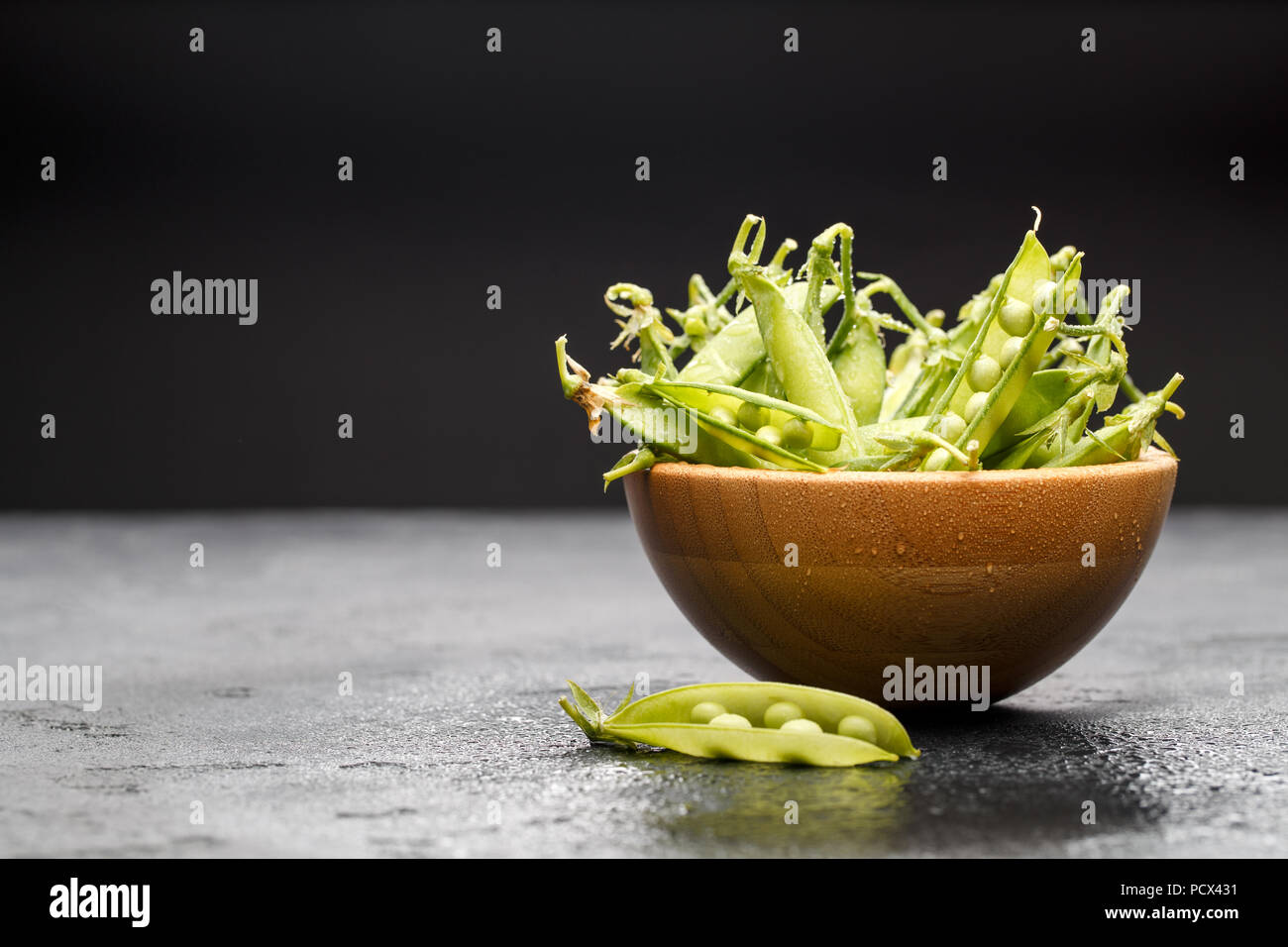 Photo of green pea pods in wooden plate on blank black table with pod ...