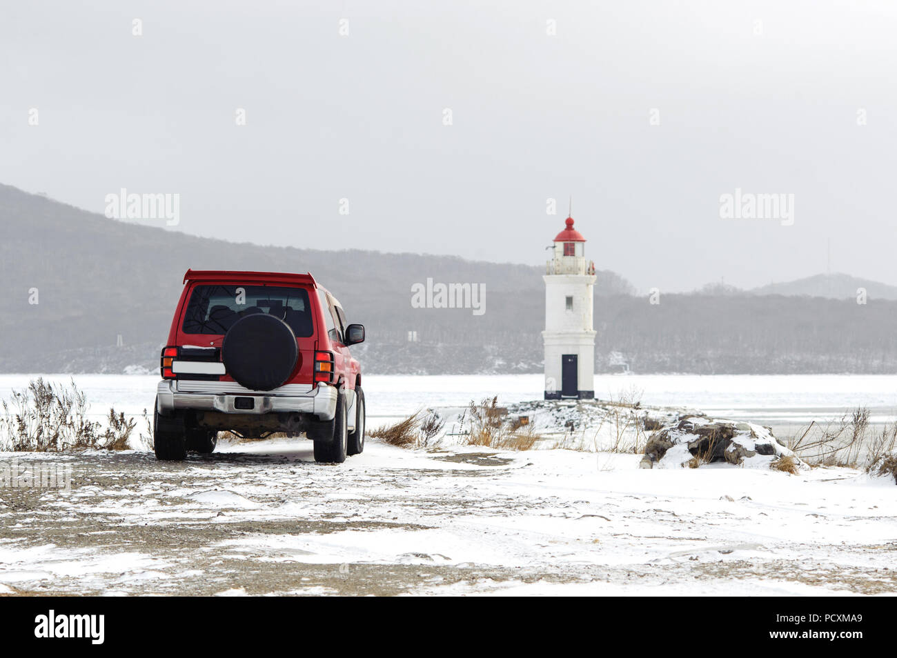 Red car in front of lighthouse on the seacoast in snowy winter day ...